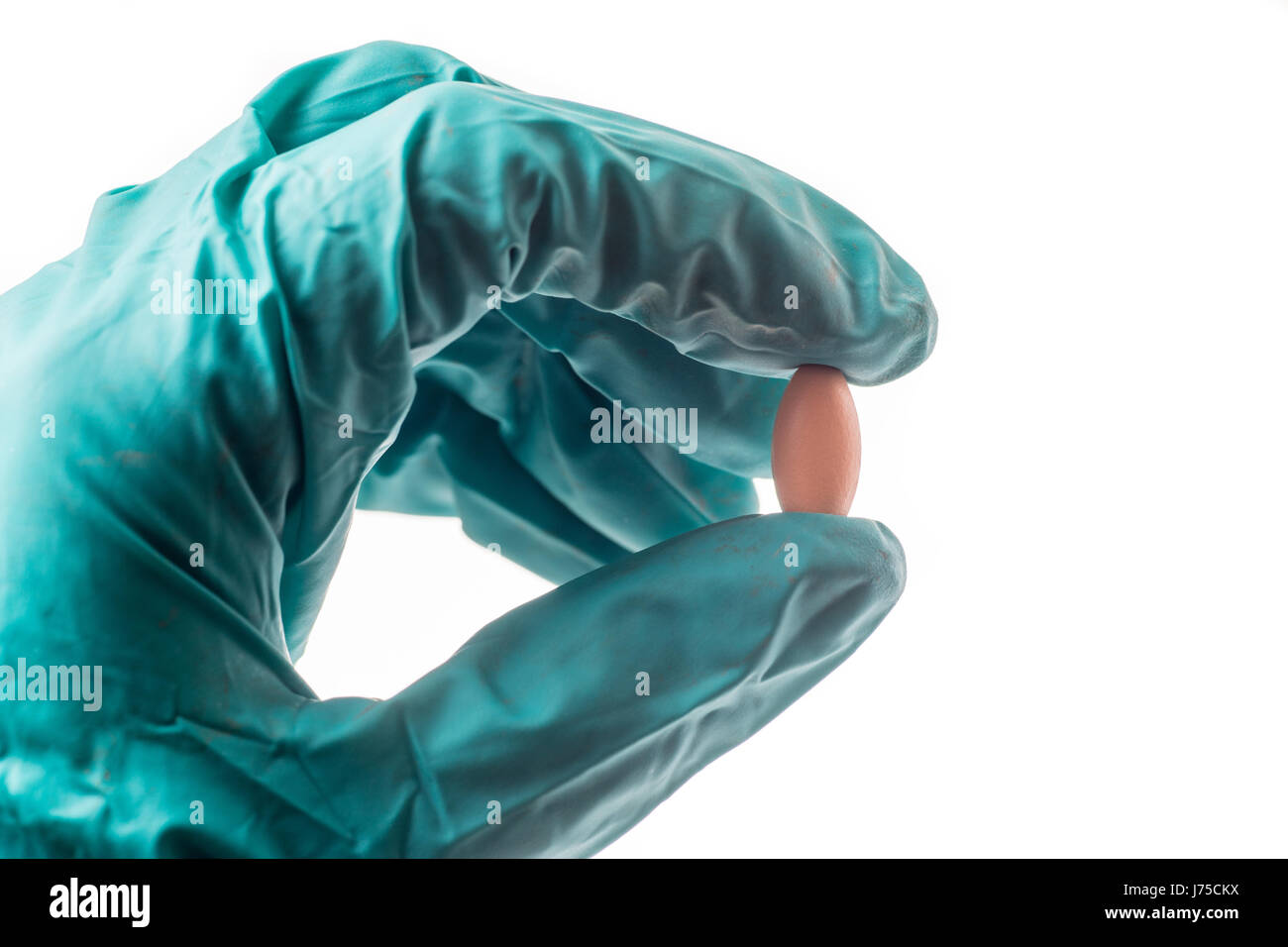 Hand with green protective glove holding an oblong pill, isolated on ...