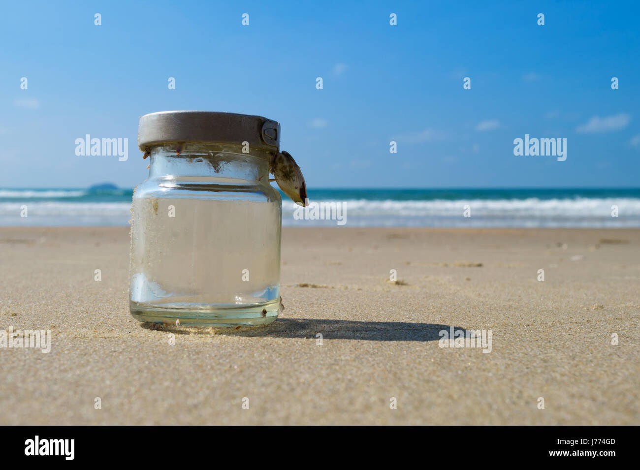 Empty glass bottle on sandy beach with blue sky and sea Stock Photo - Alamy