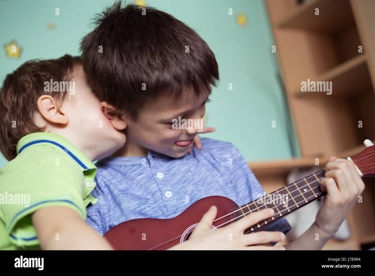 Boy playing ukulele while his little brother embracing him Stock Photo ...