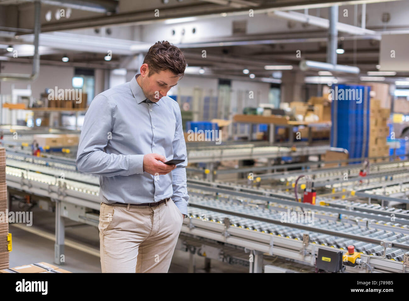 Man at conveyor belt in factory looking at cell phone Stock Photo - Alamy