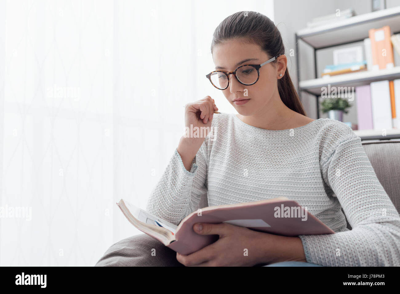 Smart female student doing homework, she is reading a book and holding ...