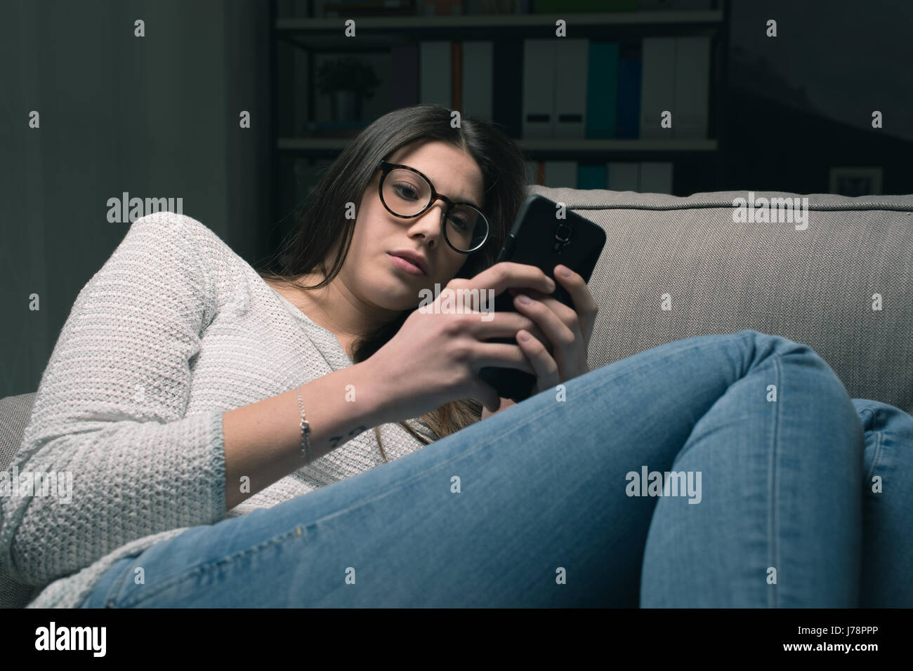 Teenager relaxing at home late at night and texting with her smartphone ...