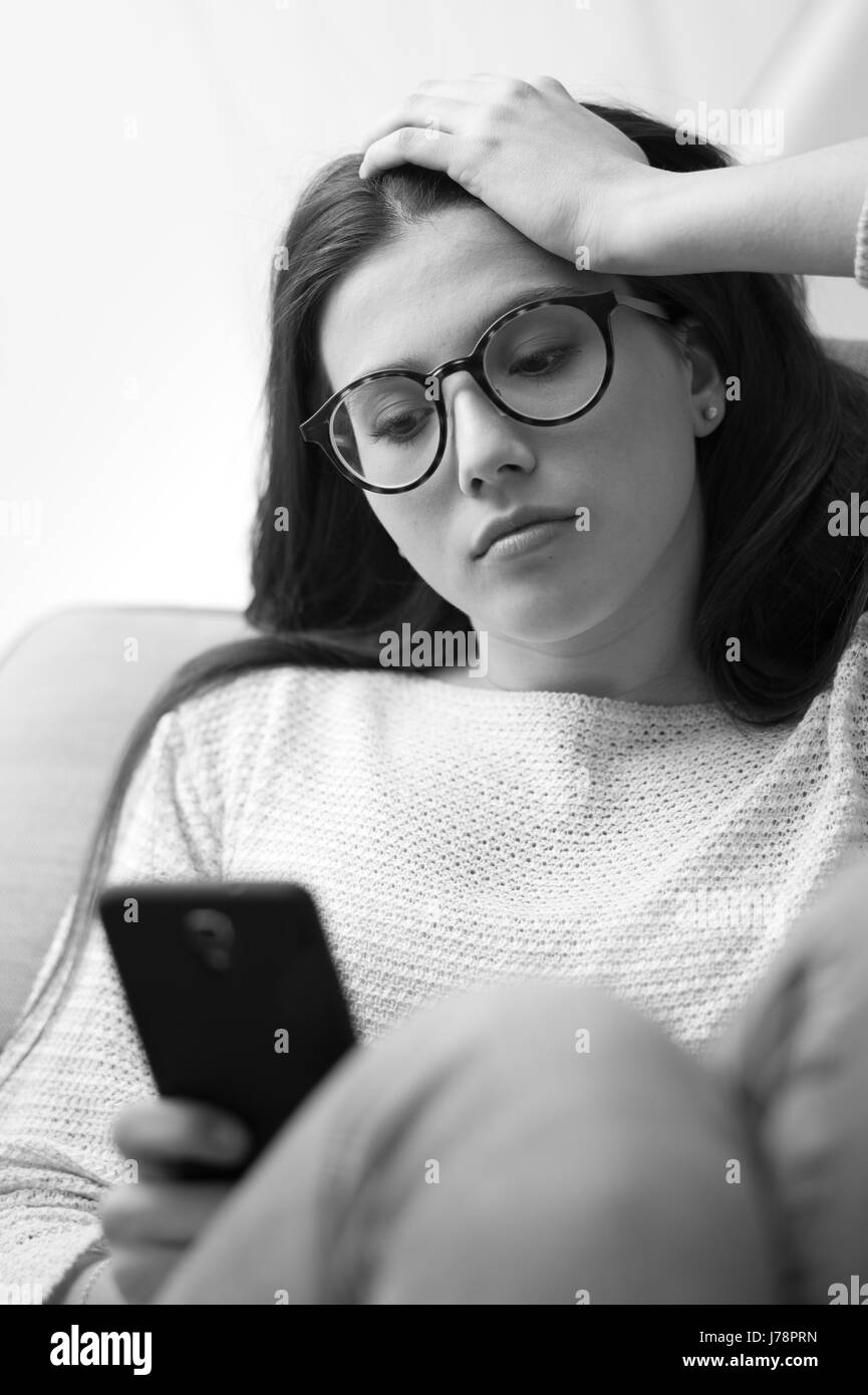 Sad young girl lying on the sofa and texting with her smartphone, she ...