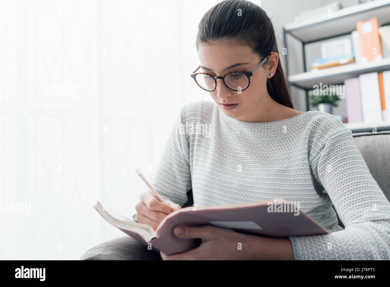 Smart female student doing homework, she is reading a book and holding ...