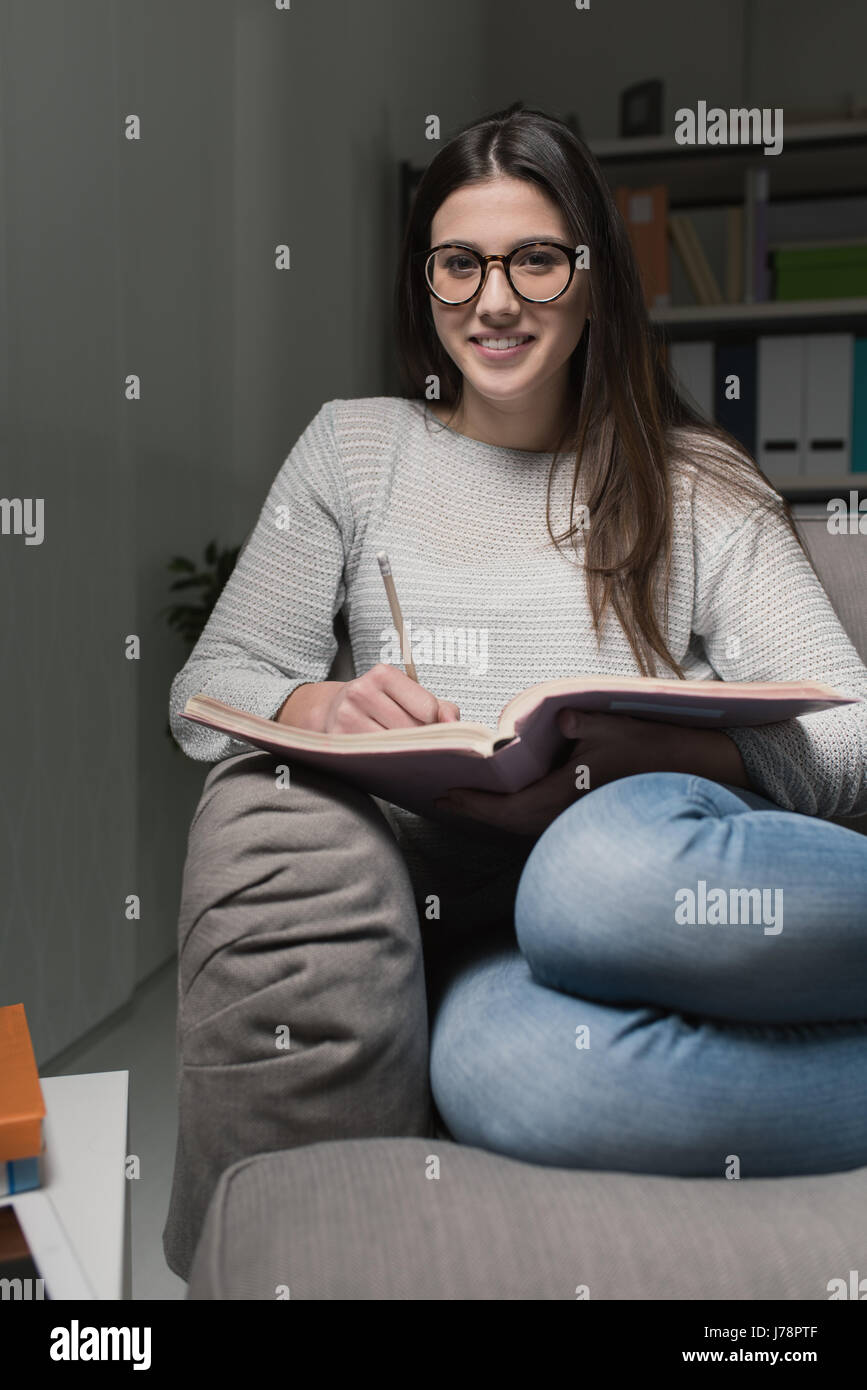 Smiling young female student doing homework late at night, she is ...