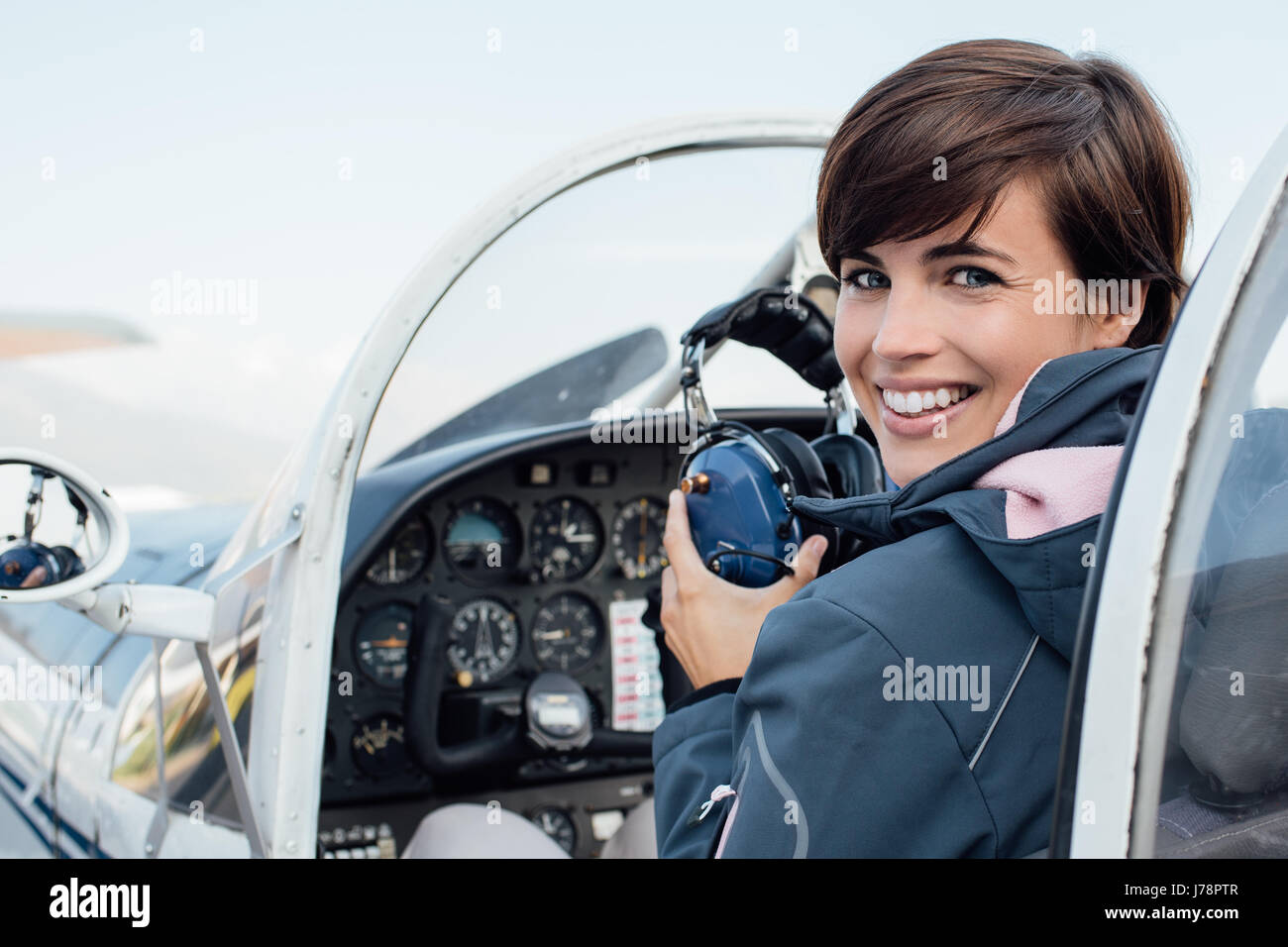 Smiling female pilot in the light aircraft cockpit, she is holding ...