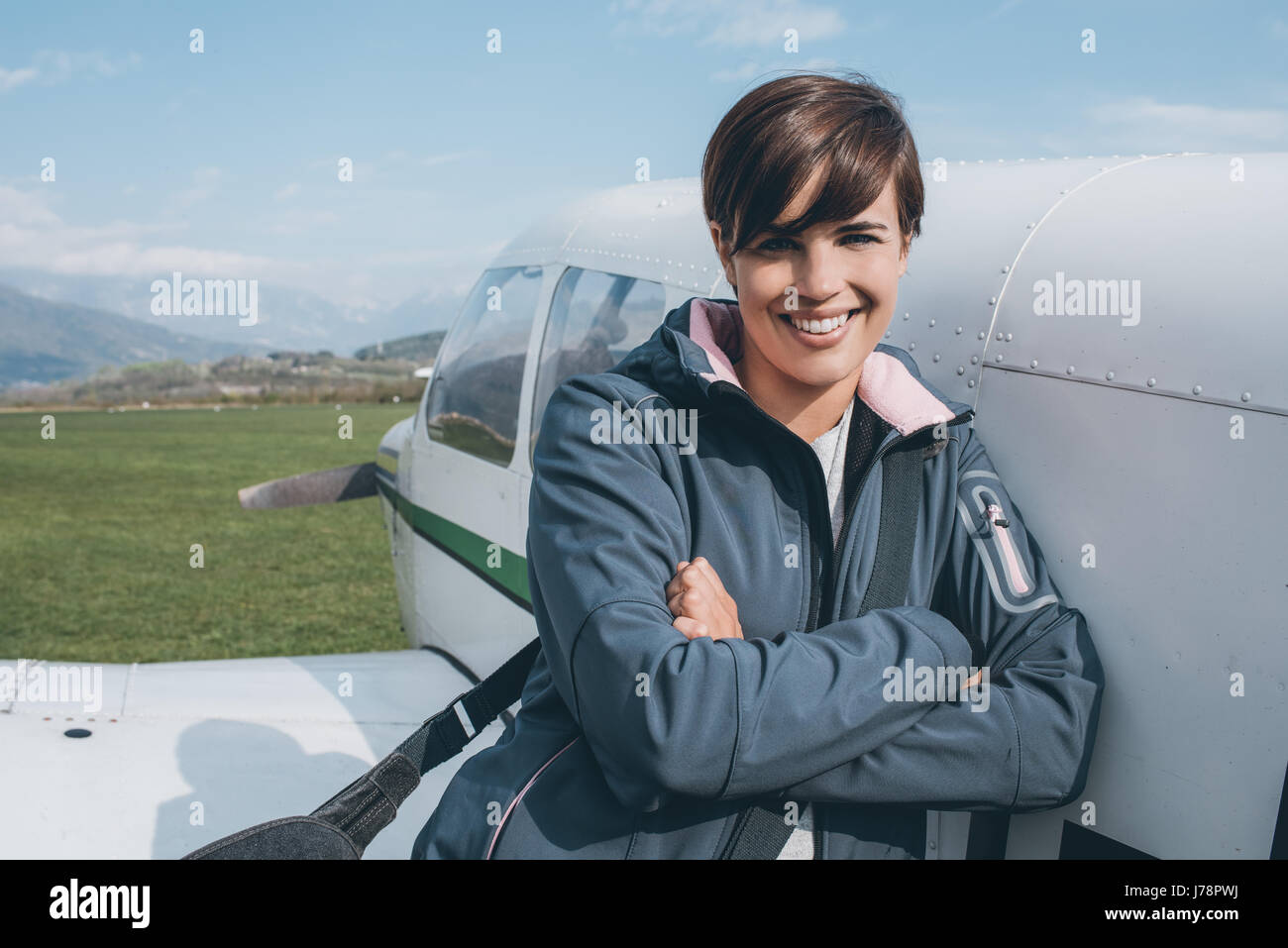 Smiling cheerful female pilot leaning on a propeller airplane and ...