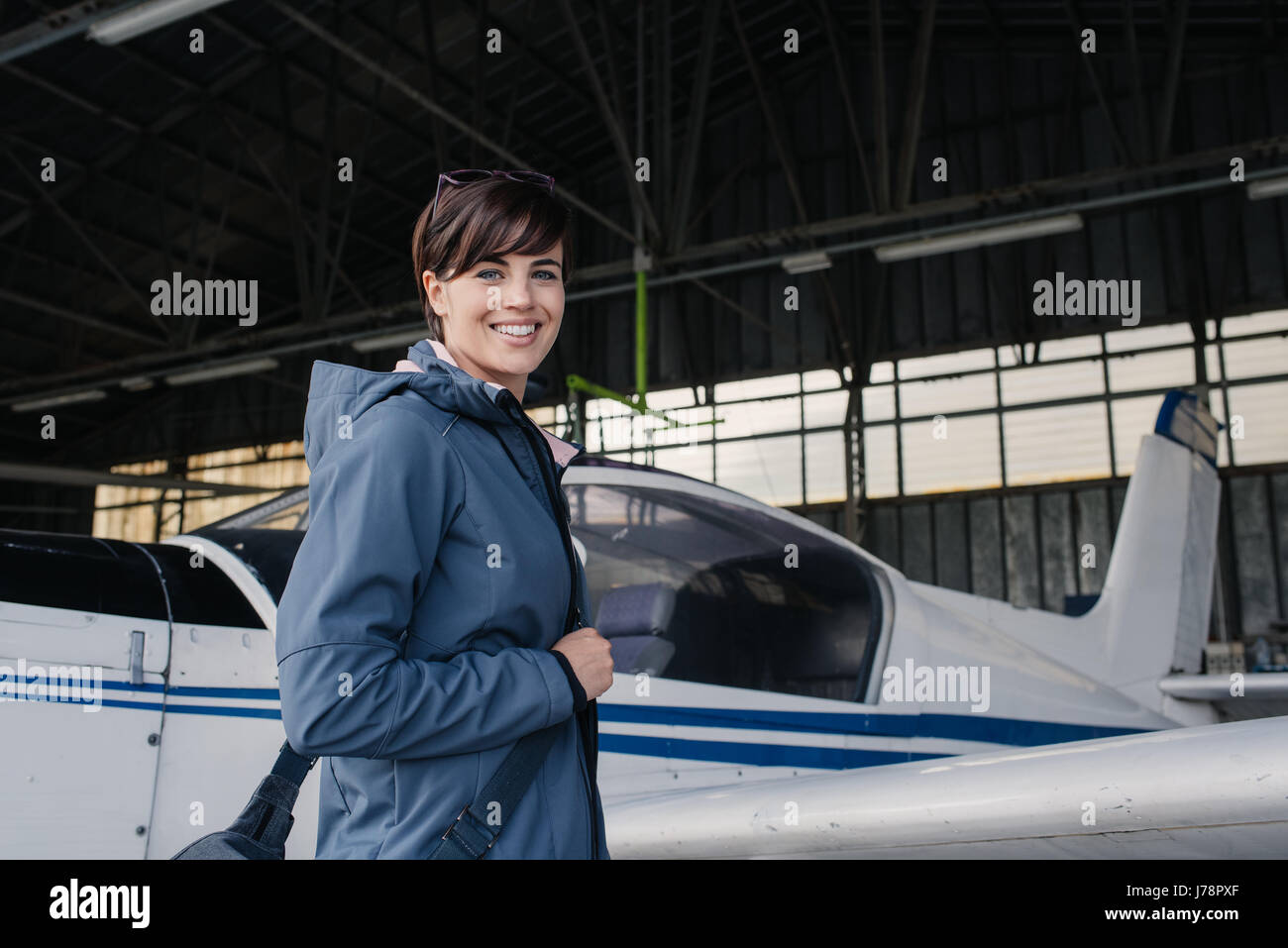 Smiling female pilot posing in the airport hangar, propeller airplane ...