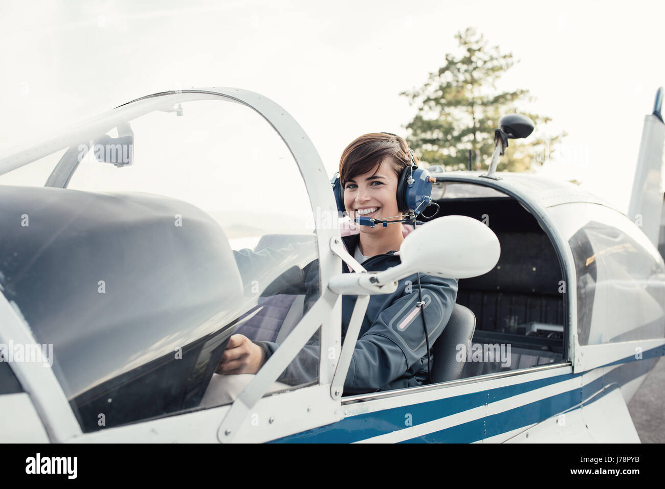 Smiling female pilot in the light aircraft cockpit, she is wearing ...