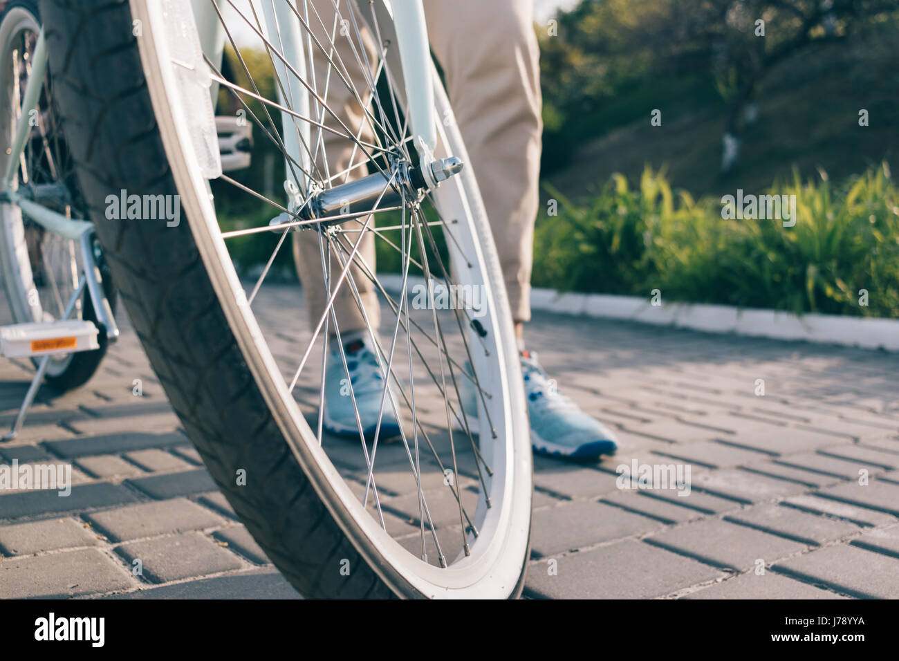 Wheel of a bicycle and female feet in sneakers close-up Stock Photo - Alamy