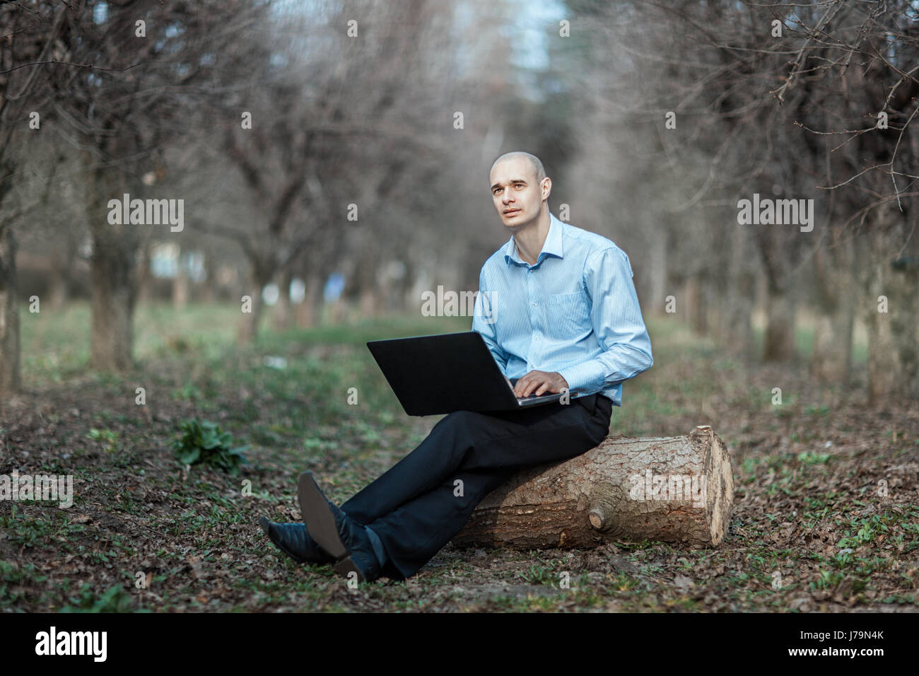 Man with a dreaming face working at a laptop in the park. He looks ...