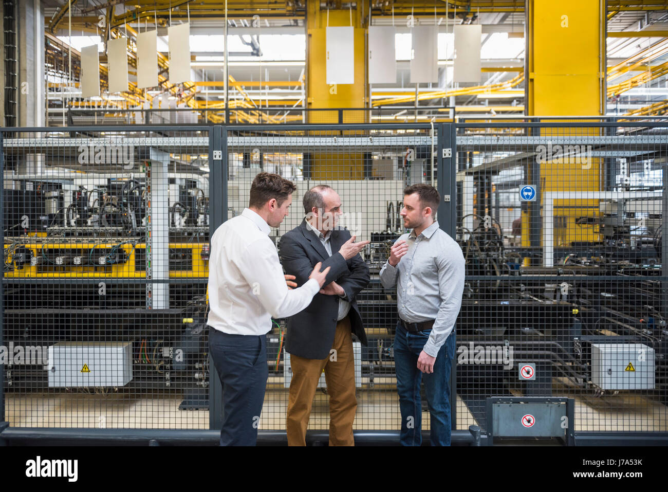 Three men talking in factory shop floor Stock Photo - Alamy