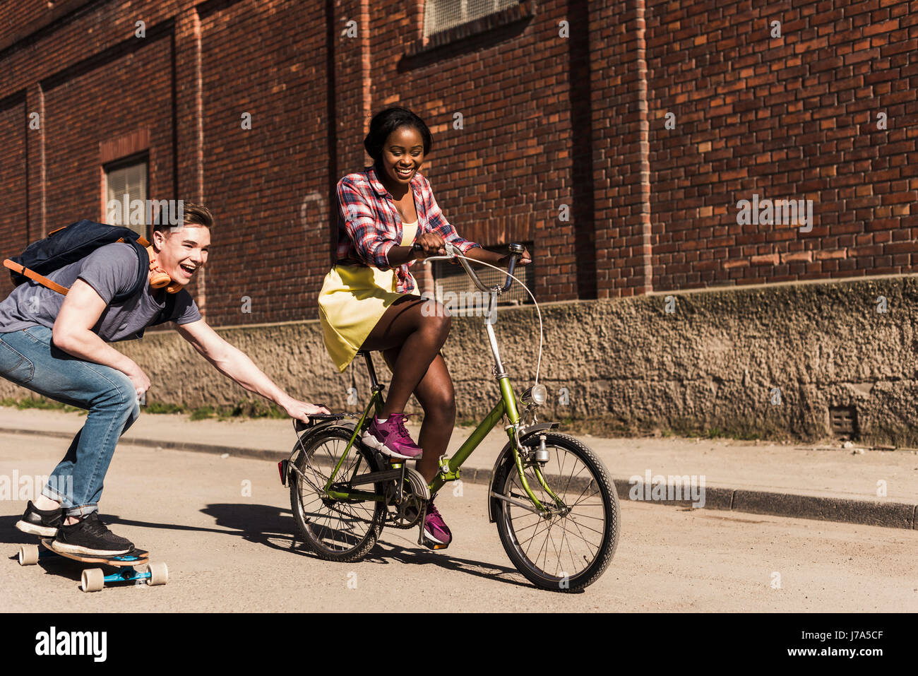Young woman on bicycle pulling young man, standing on skateboard Stock ...