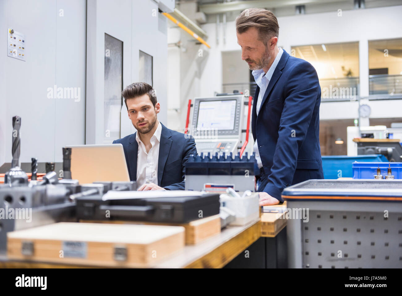 Two men at table in factory using laptop Stock Photo - Alamy