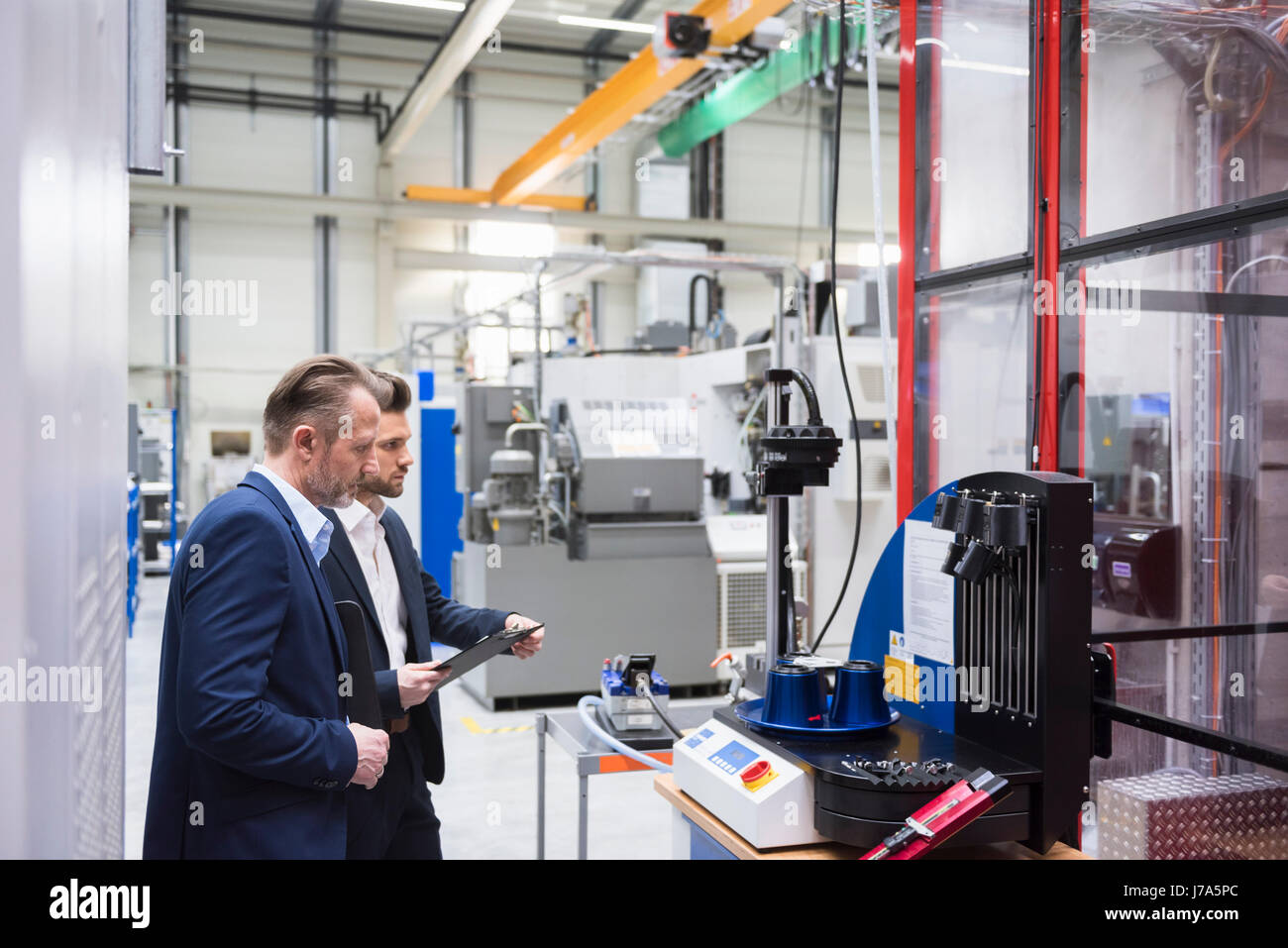 Two businessmen in factory shop floor examining machine Stock Photo - Alamy