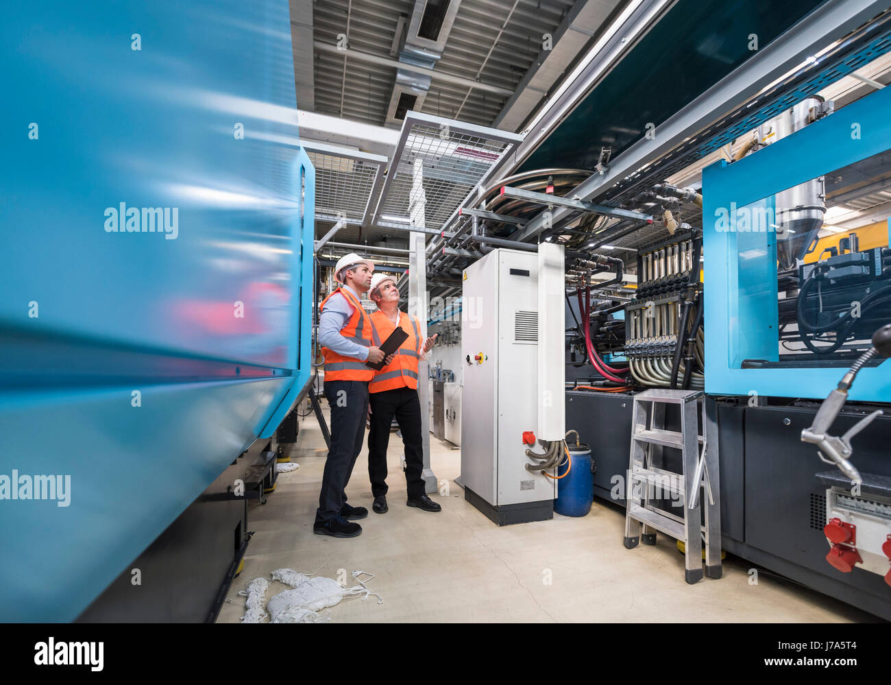 Two men wearing safety vests and hard hats examining system in factory ...