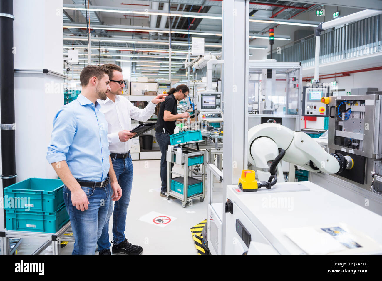 Two men talking in factory shop floor with man in background working ...