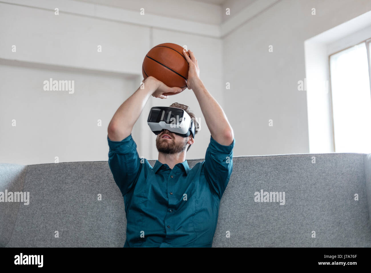 Young man with basketball sitting on couch using Virtual Reality ...