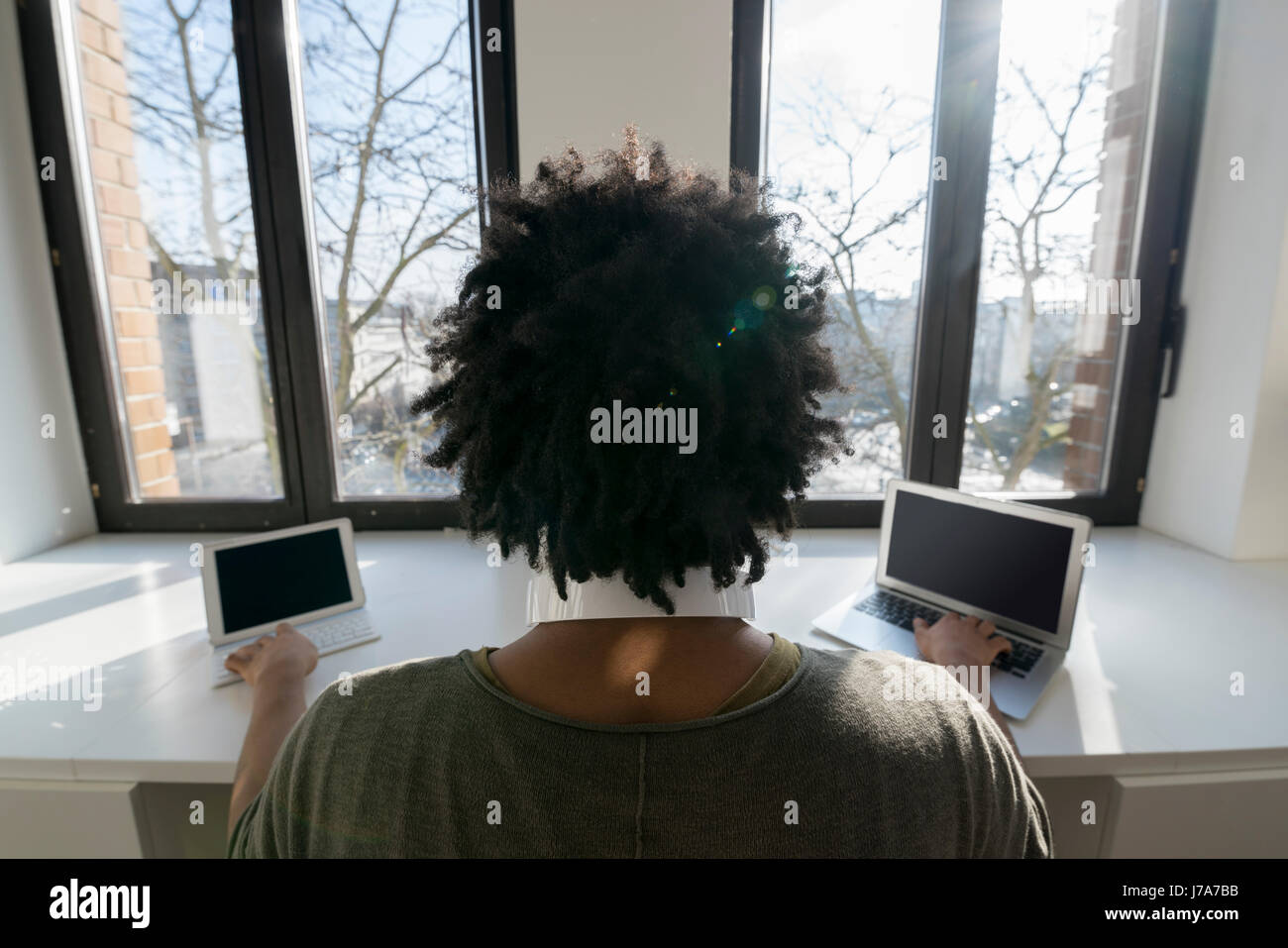 Man working in front of panorama window at home with laptop and tablet ...