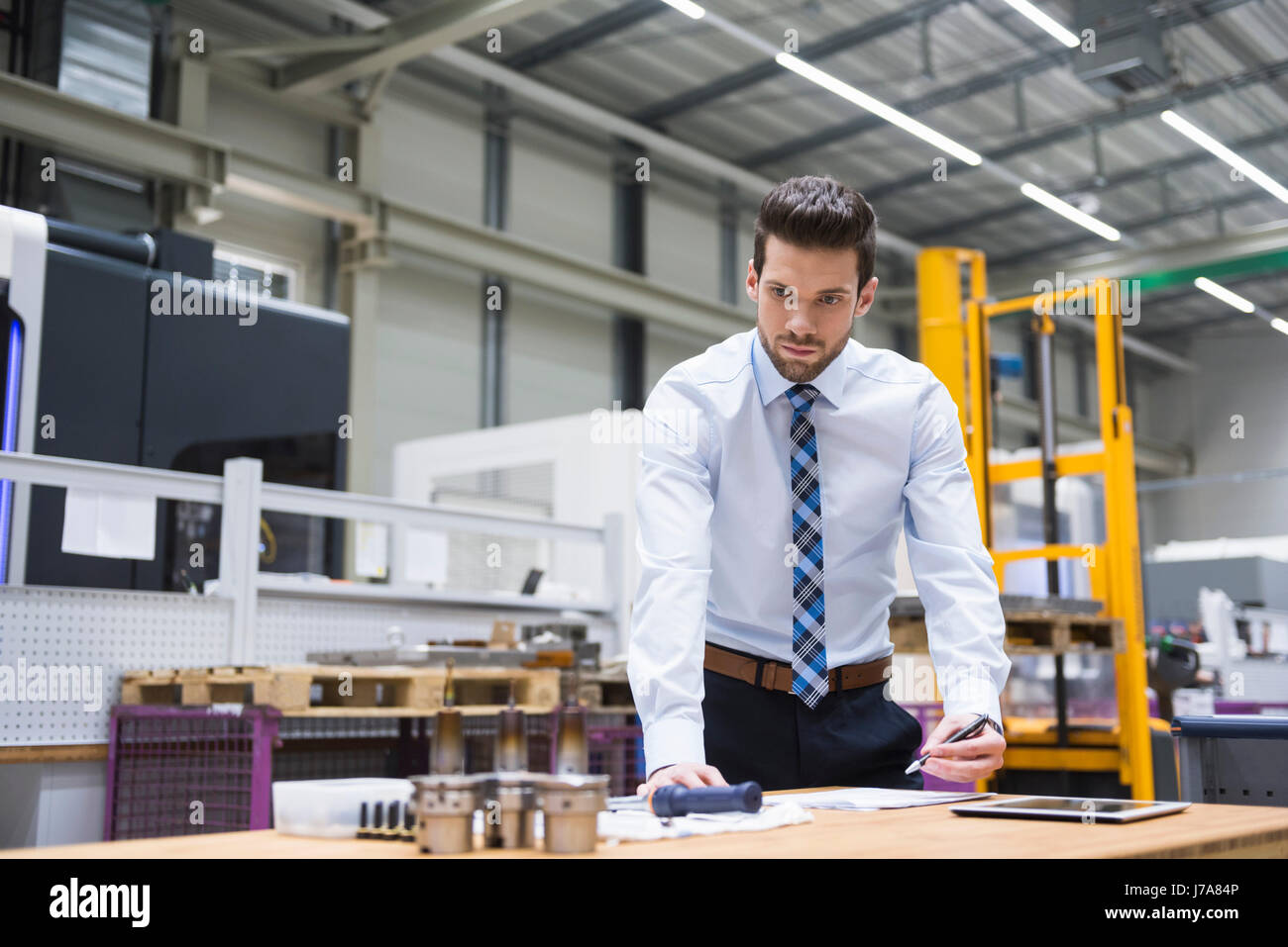 Man at table in factory shop floor taking notes Stock Photo - Alamy