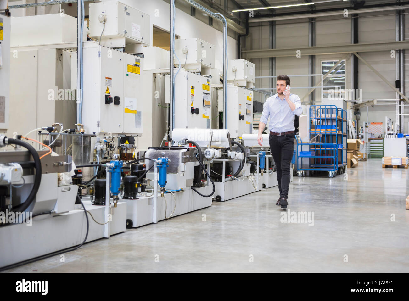 Man walking in factory shop floor talking on the phone Stock Photo - Alamy
