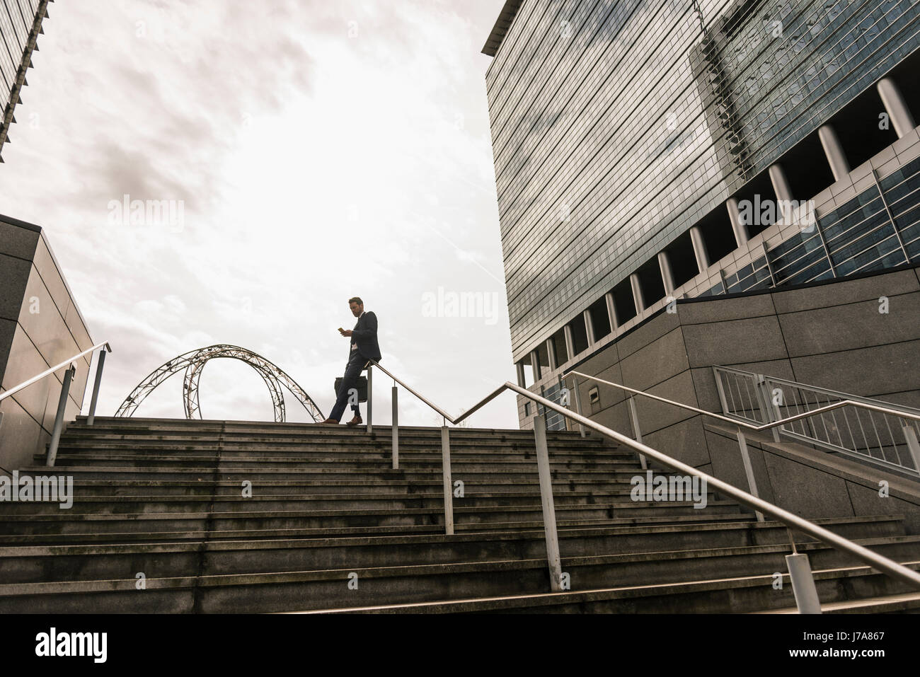 Businessman leaning on railing on top of stairs reading messages Stock ...
