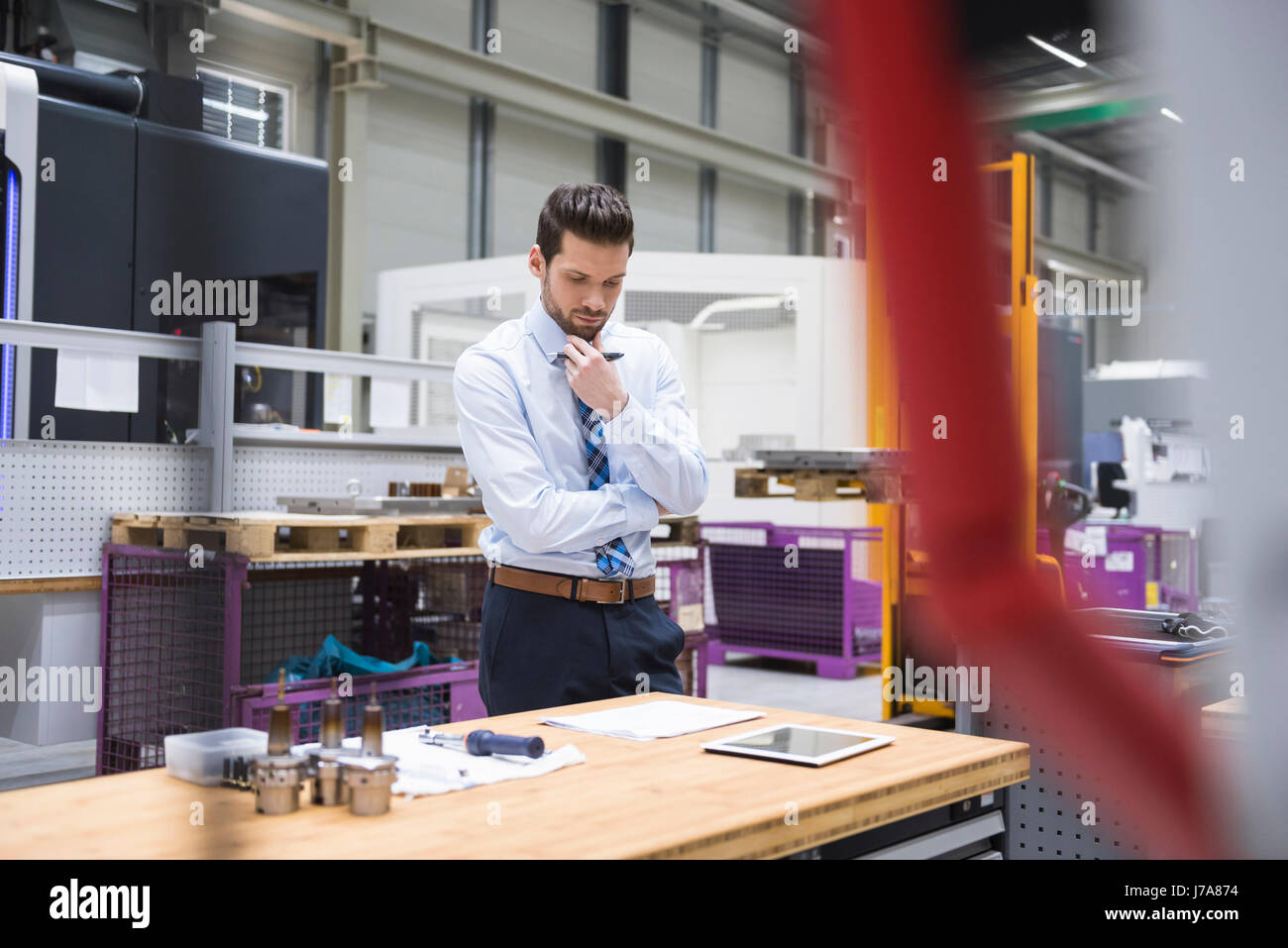 Man at table in factory shop floor thinking Stock Photo - Alamy