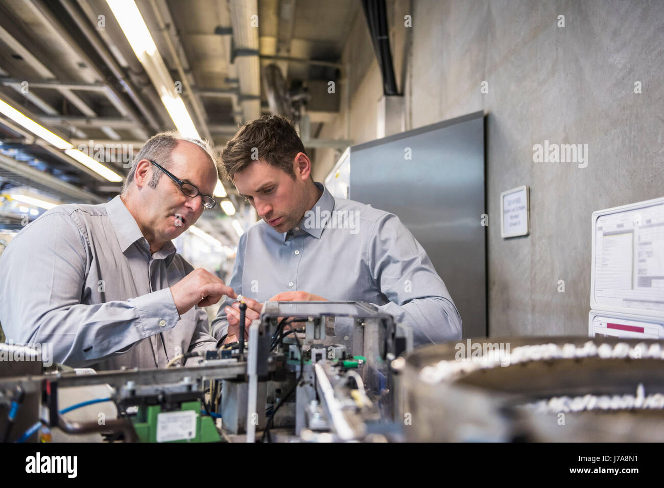 Two men in factory shop floor examining outcome of a machine Stock ...