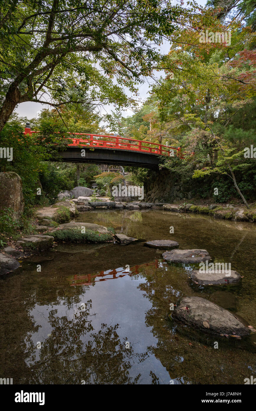 A red and black bridge on Miyajima island. Both foliage and bridge are ...
