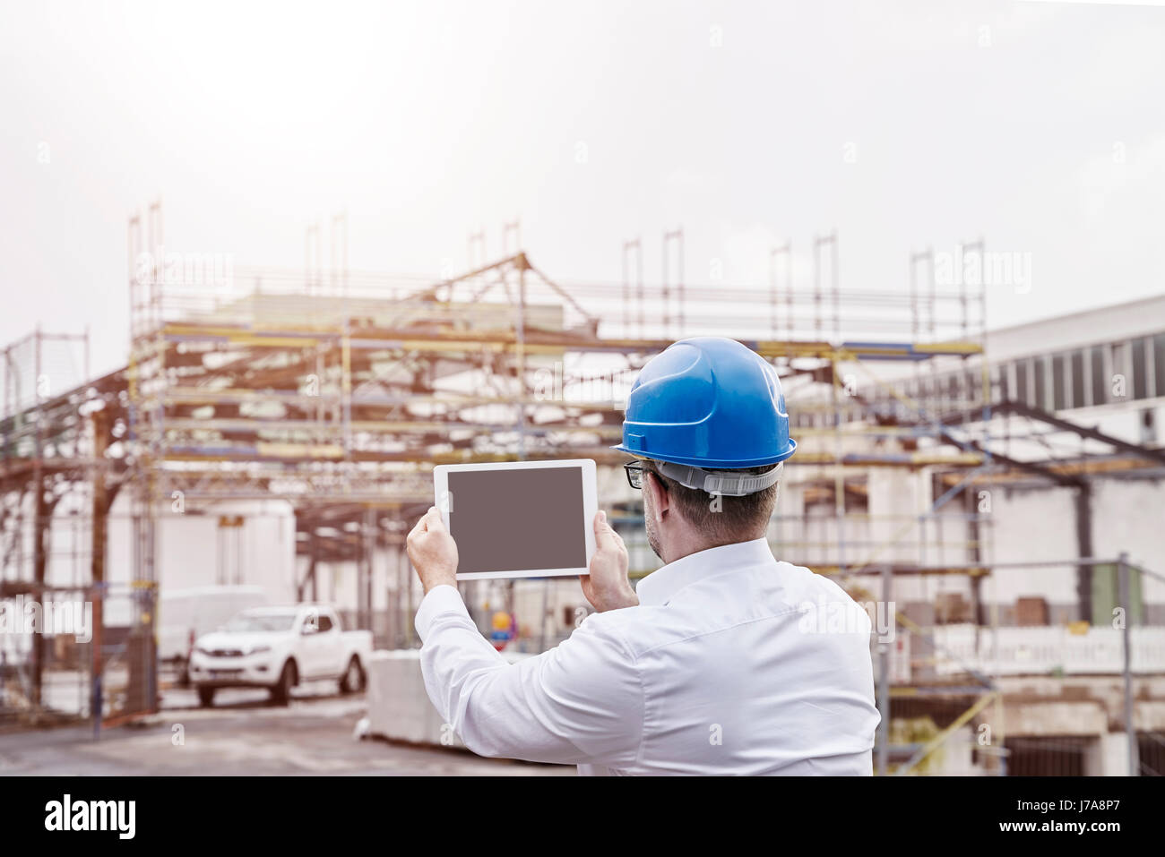 Back view of man wearing blue hart hat taking picture with tablet at ...