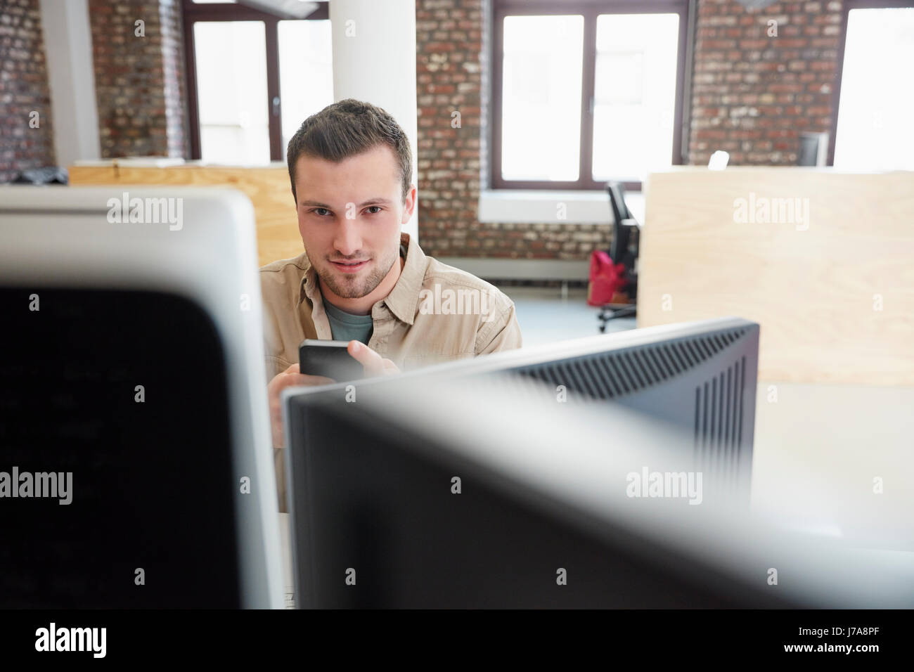 Young man sitting in office using computer and smart phone Stock Photo ...