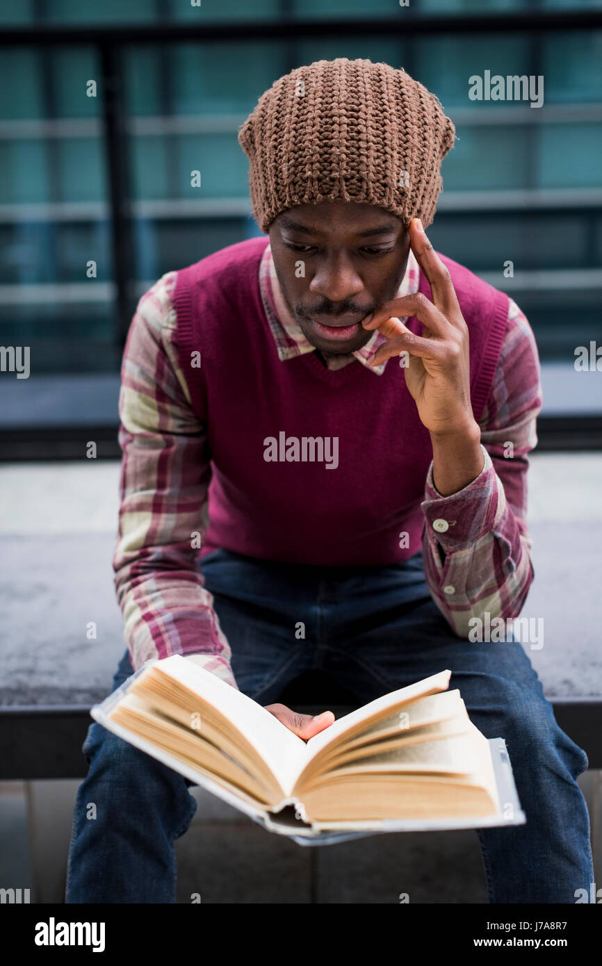 Man sitting on bench reading a book Stock Photo - Alamy