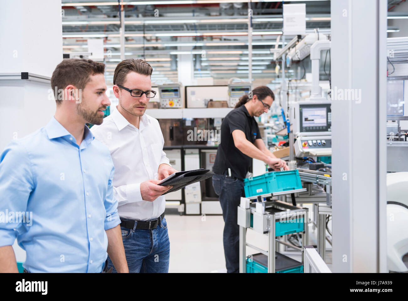 Two men talking in factory shop floor with man in background working ...