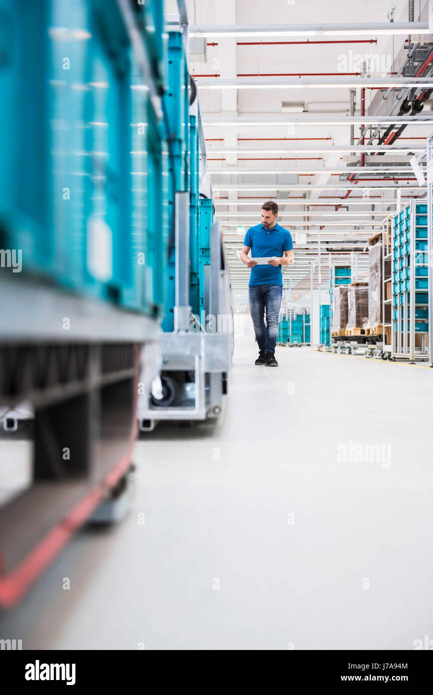 Man with tablet walking at tugger train in industrial hall Stock Photo ...