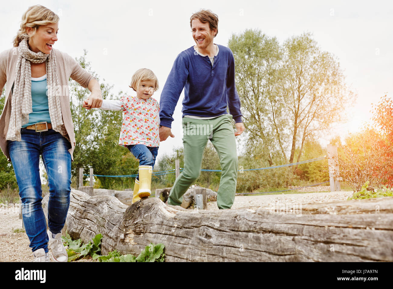 Girl balancing on a log supported by parents Stock Photo - Alamy