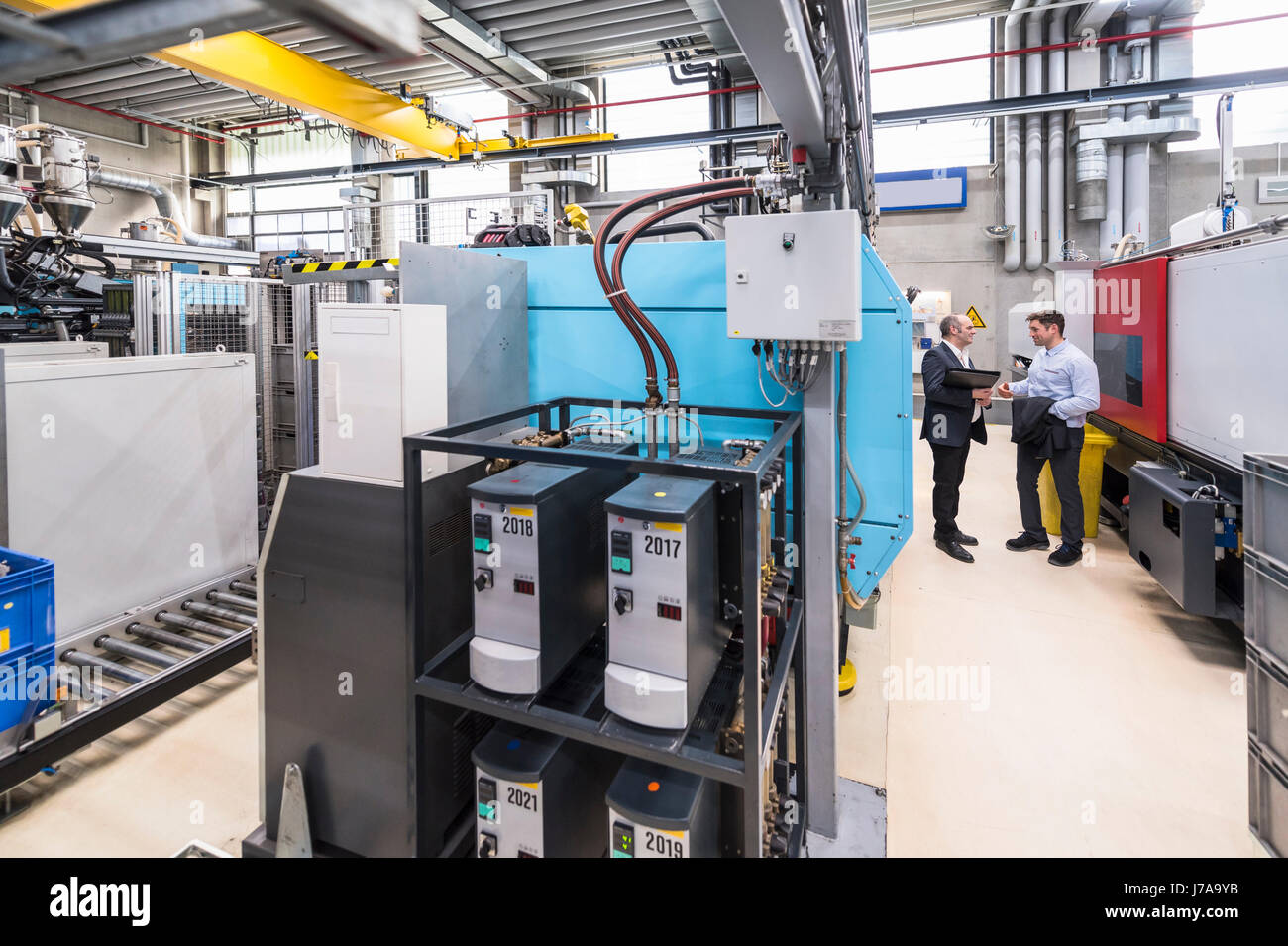 Two men talking among machines in factory shop floor Stock Photo - Alamy