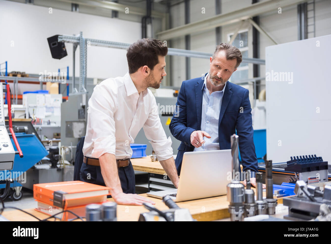 Two men at table in factory shop floor with laptop Stock Photo - Alamy