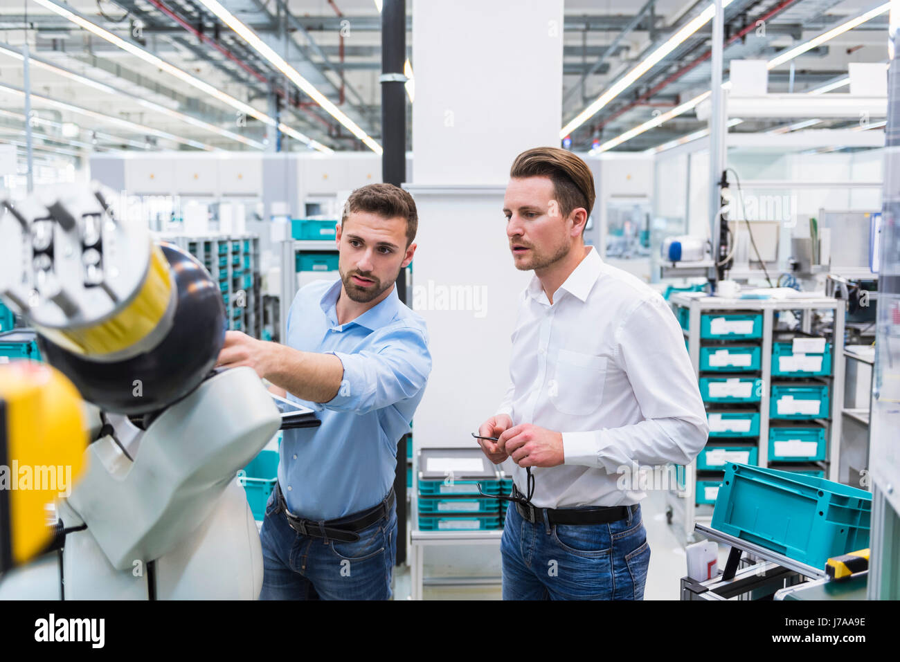 Two men with tablet examining assembly robot in factory shop floor ...