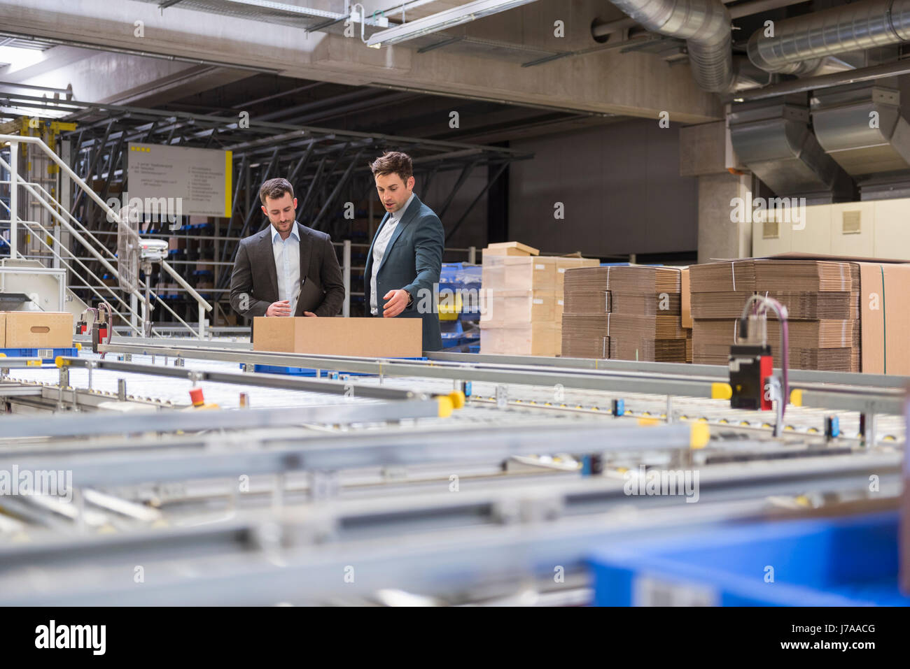 Two businessmen talking at conveyor belt in factory Stock Photo - Alamy