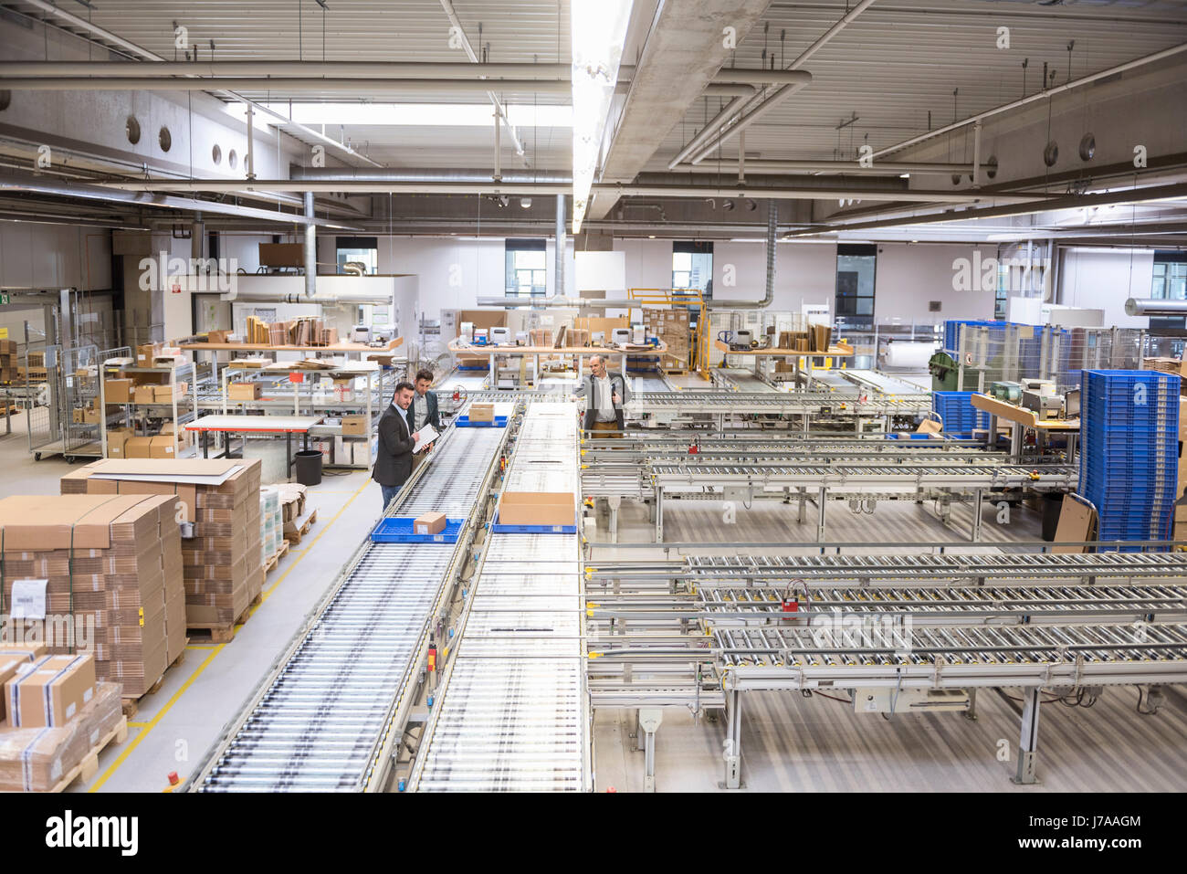 Three businessmen at conveyor belt in factory Stock Photo - Alamy