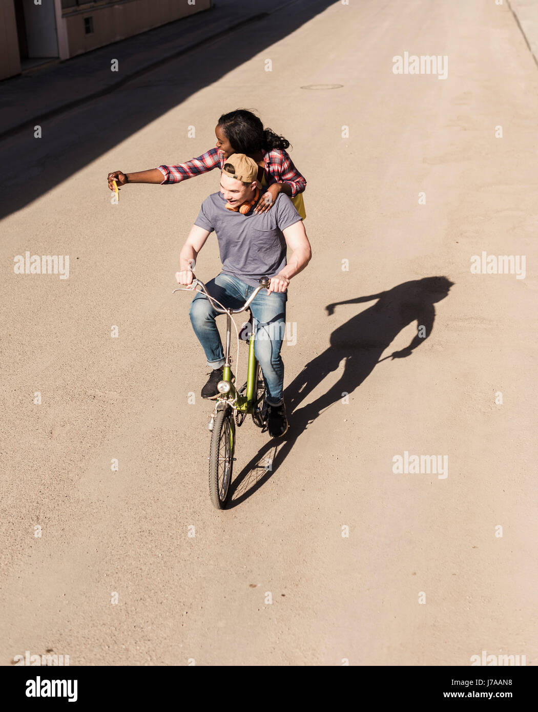 Young man riding bicycle with his girlfriend standing on rack, taking ...