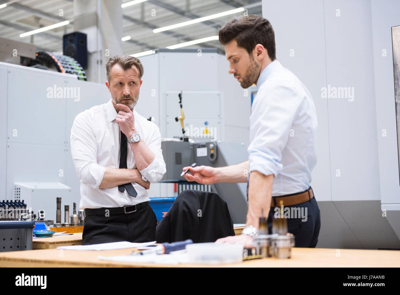 Two businessmen at table in factory shop floor discussing Stock Photo ...