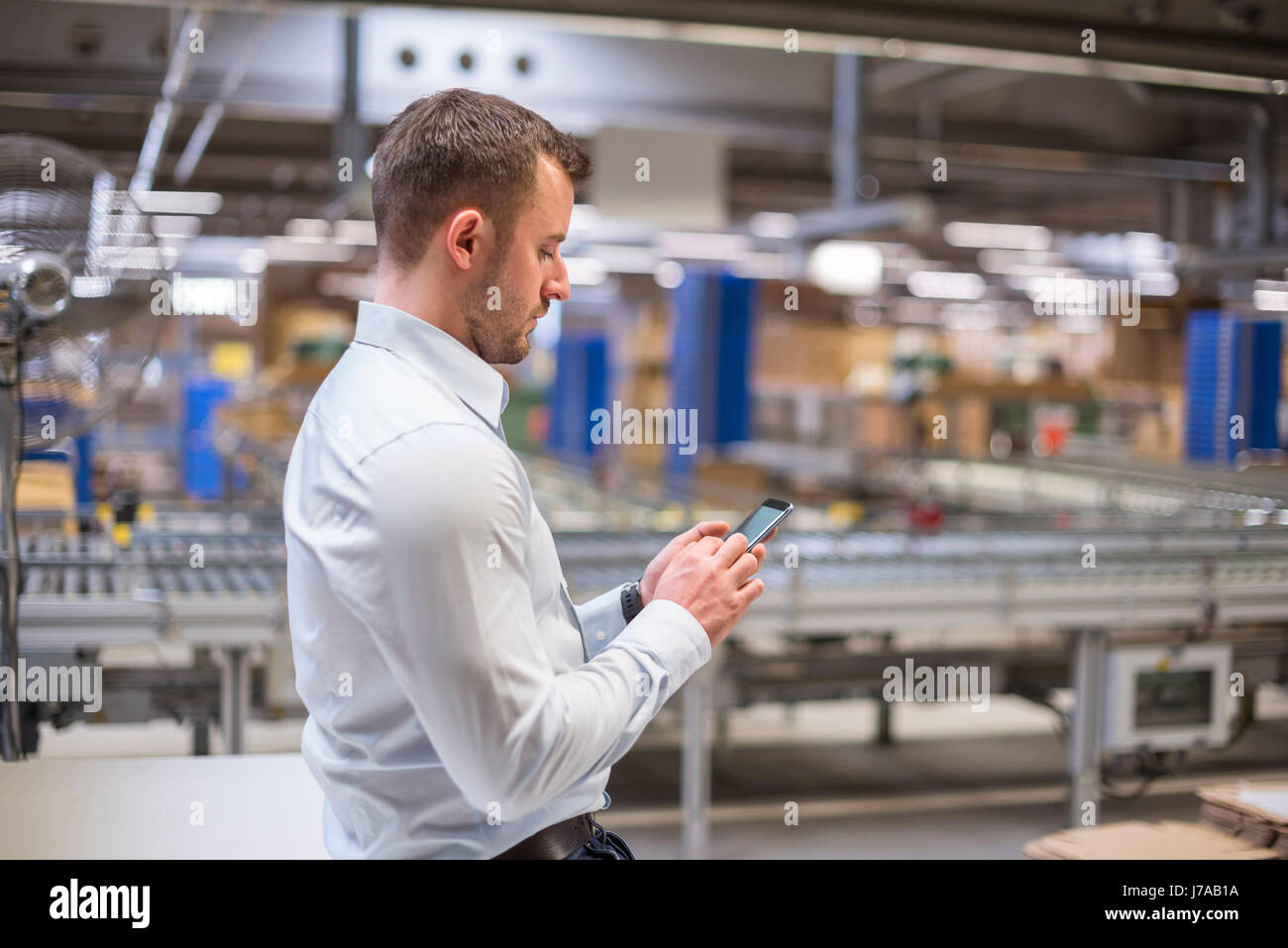 Man in factory looking at cell phone Stock Photo - Alamy