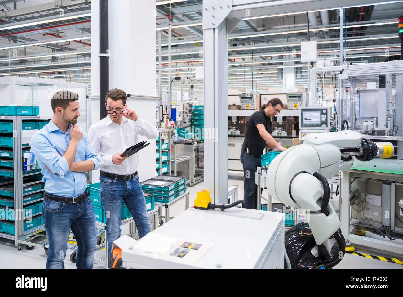 Man operating assembly robot in factory and two men talking Stock Photo ...