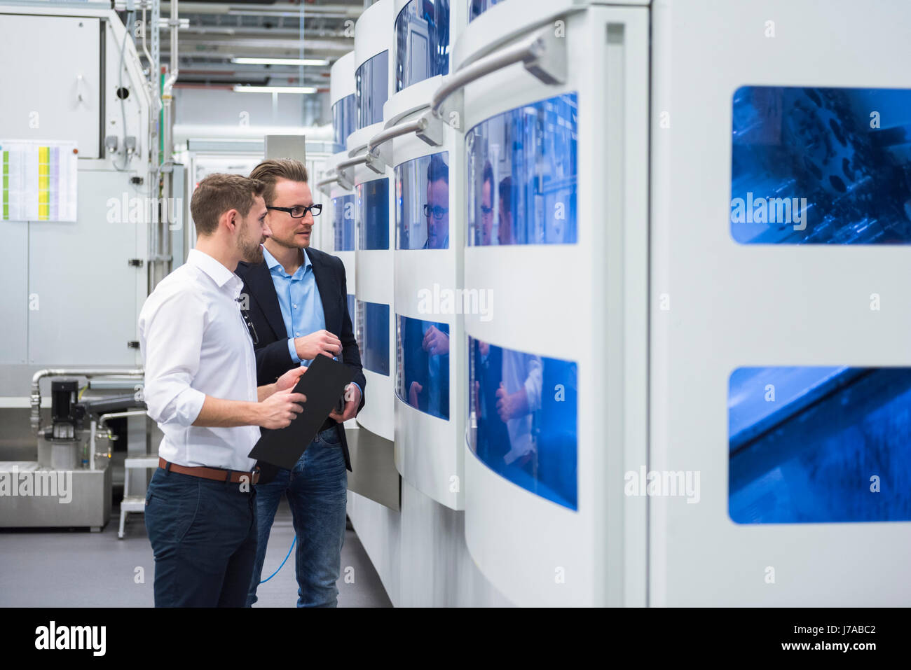 Two men talking in factory shop floor looking at machine Stock Photo ...