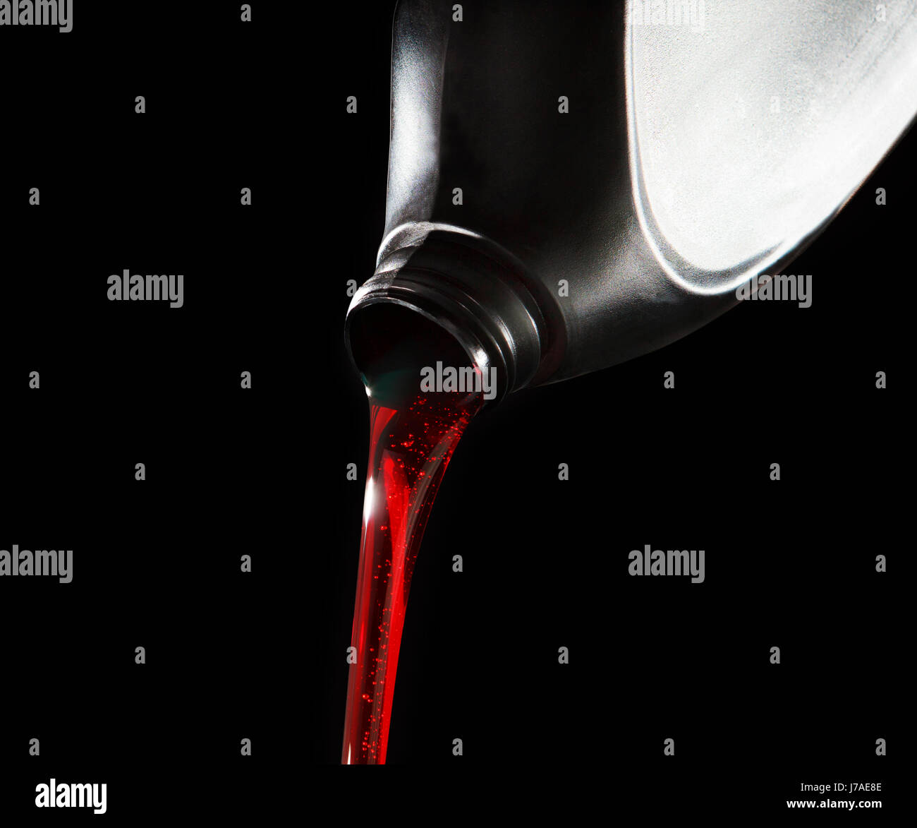 file close up red motor oil pouping from black plastic bottle against ...