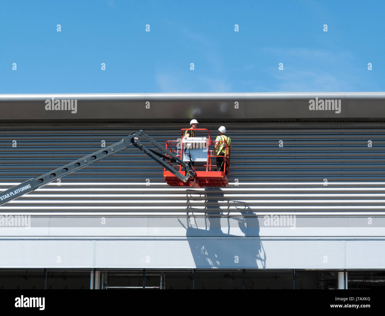 construction workers on mobile access platform installing on cladding ...