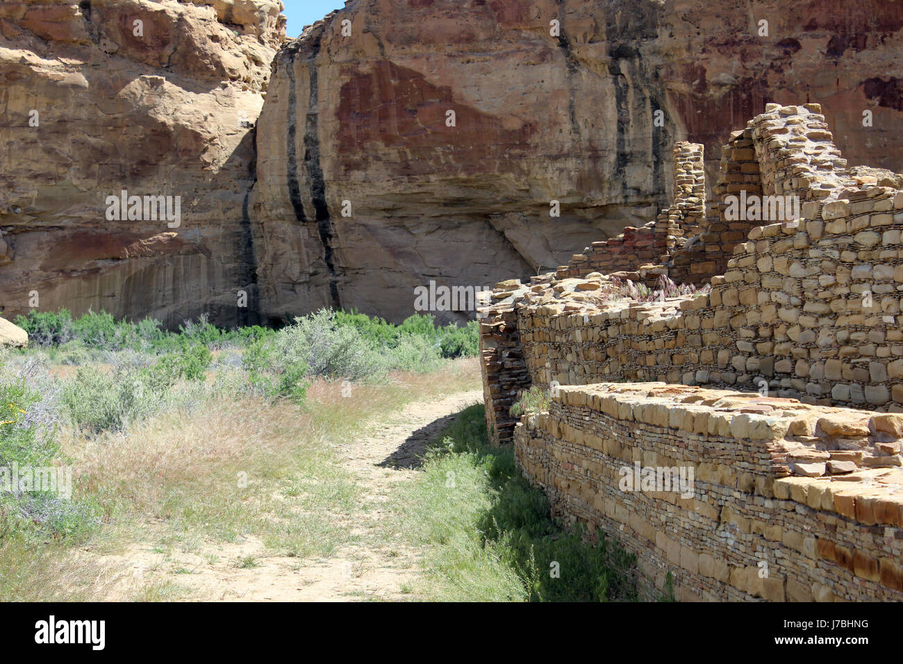 An ancient stone wall stands next to a path with cliffs behind and ...