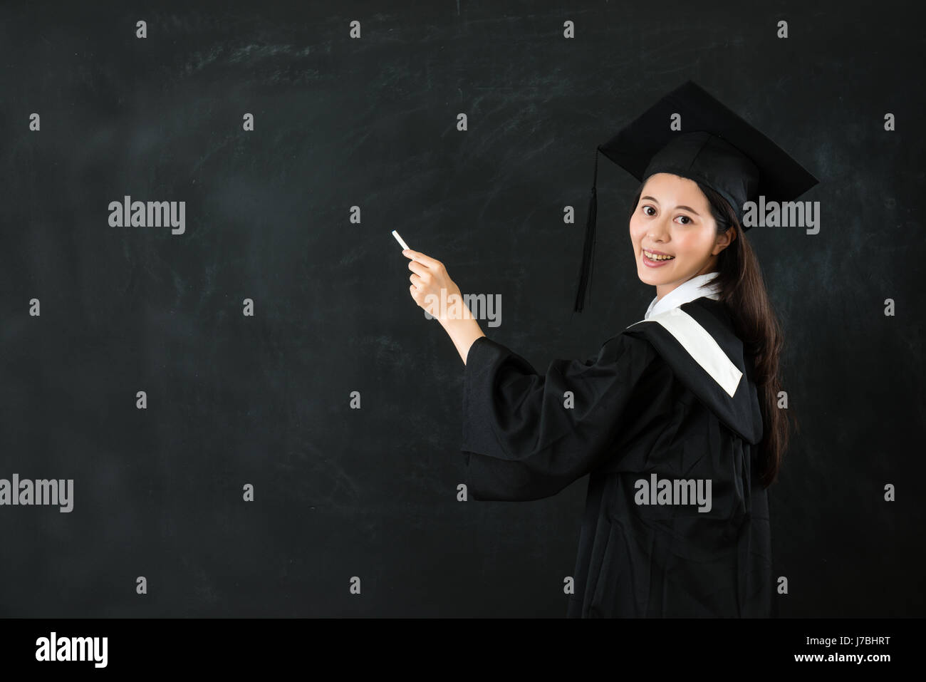 happy female student holding chalk looking back smiling stand in front ...