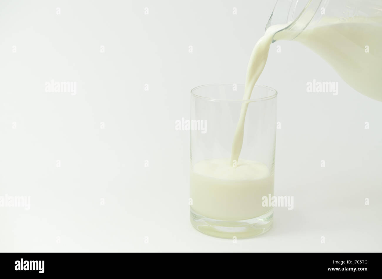 Milk in a jar on a light background is poured into a glass Stock Photo ...